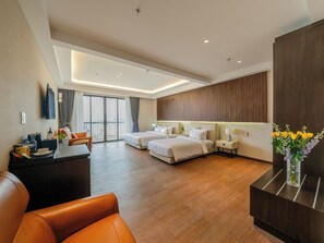 Quarto de hotel com duas camas, uma escrivaninha, um espaço de estar e uma janela grande.
