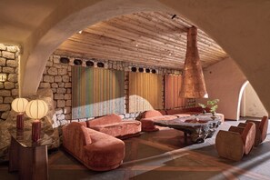 Ambiente acolhedor com paredes de pedra, teto de madeira e área de estar com sofás e uma mesa de centro.