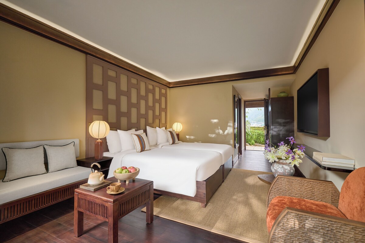 Quarto de hotel com cama, sofá e uma pequena mesa com uma tigela de frutas.