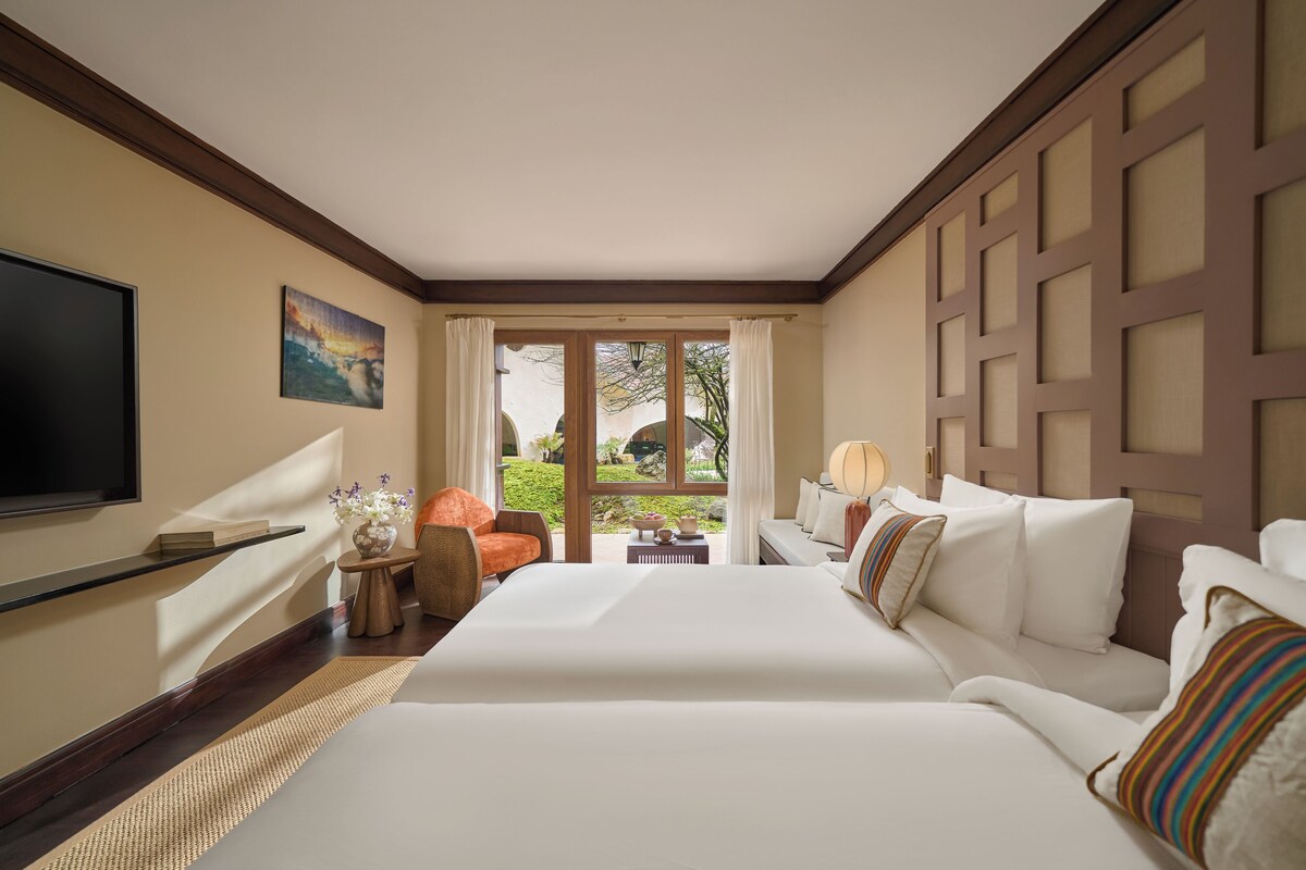 Quarto de hotel com uma cama grande, televisão, pintura e vista para o exterior.