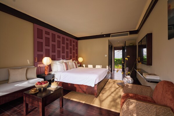 Quarto de hotel com cama, sofá, mesa de centro e mesa de jantar. Há uma janela com vista para áreas verdes.