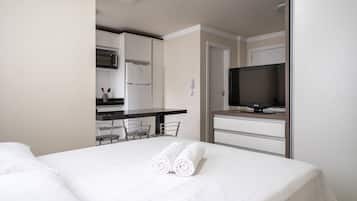 Quarto de hotel com cama, televisão, cozinha compacta e área de refeições.