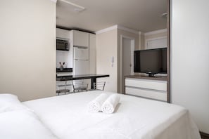Quarto de hotel com cama, televisão, cozinha compacta e área de refeições.