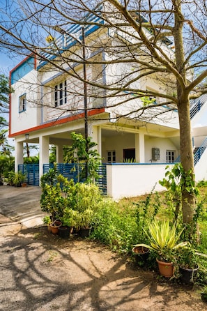 Um edifício de dois andares com varanda coberta, plantas em vasos e cerca azul.
