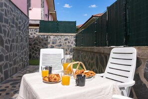 Uma área de refeições ao ar livre com uma mesa posta para o café da manhã, incluindo croissants, suco de laranja e um cesto de pretzels.