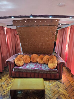 Um sofá de couro marrom com encosto estofado e almofadas decorativas, uma almofada estampada e uma mesa de madeira à frente.