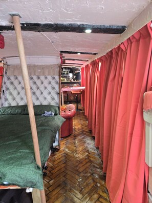 Quarto com beliche, mesa pequena com cadeiras, área de bar e cortinas vermelhas.