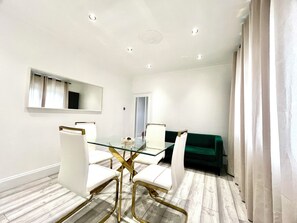 Uma sala de jantar moderna com mesa de vidro, cadeiras brancas e um sofá verde.