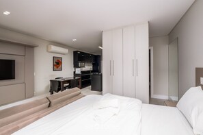 Quarto de hotel moderno com uma cama grande, um sofá, uma mesa de escritório e uma cozinha compacta.