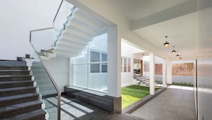 Interior moderno com escadaria de vidro, vista para um jardim e corredor com iluminação no teto.