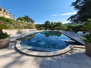 Piscina retangular com deck revestido, rodeada por espreguiçadeiras e plantas em vasos.