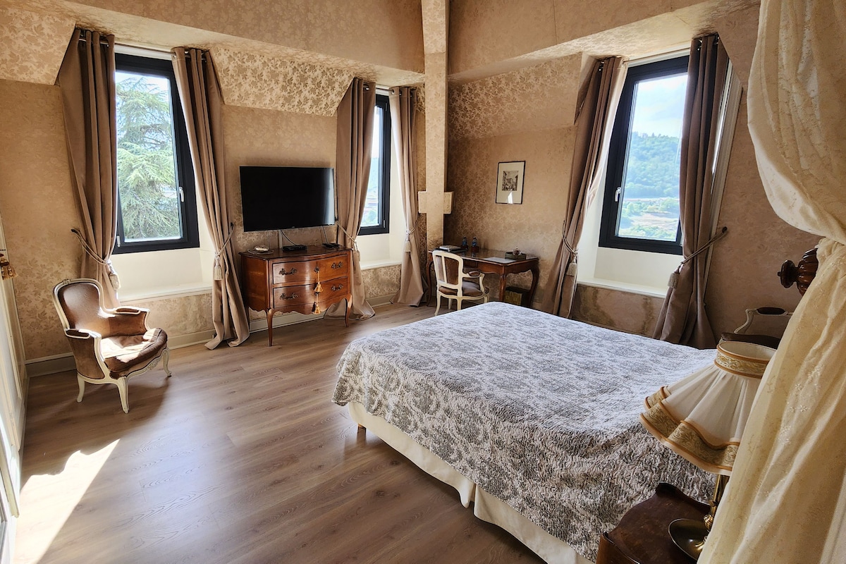 Quarto com cama, escrivaninha, cadeira, televisão e cortinas.
