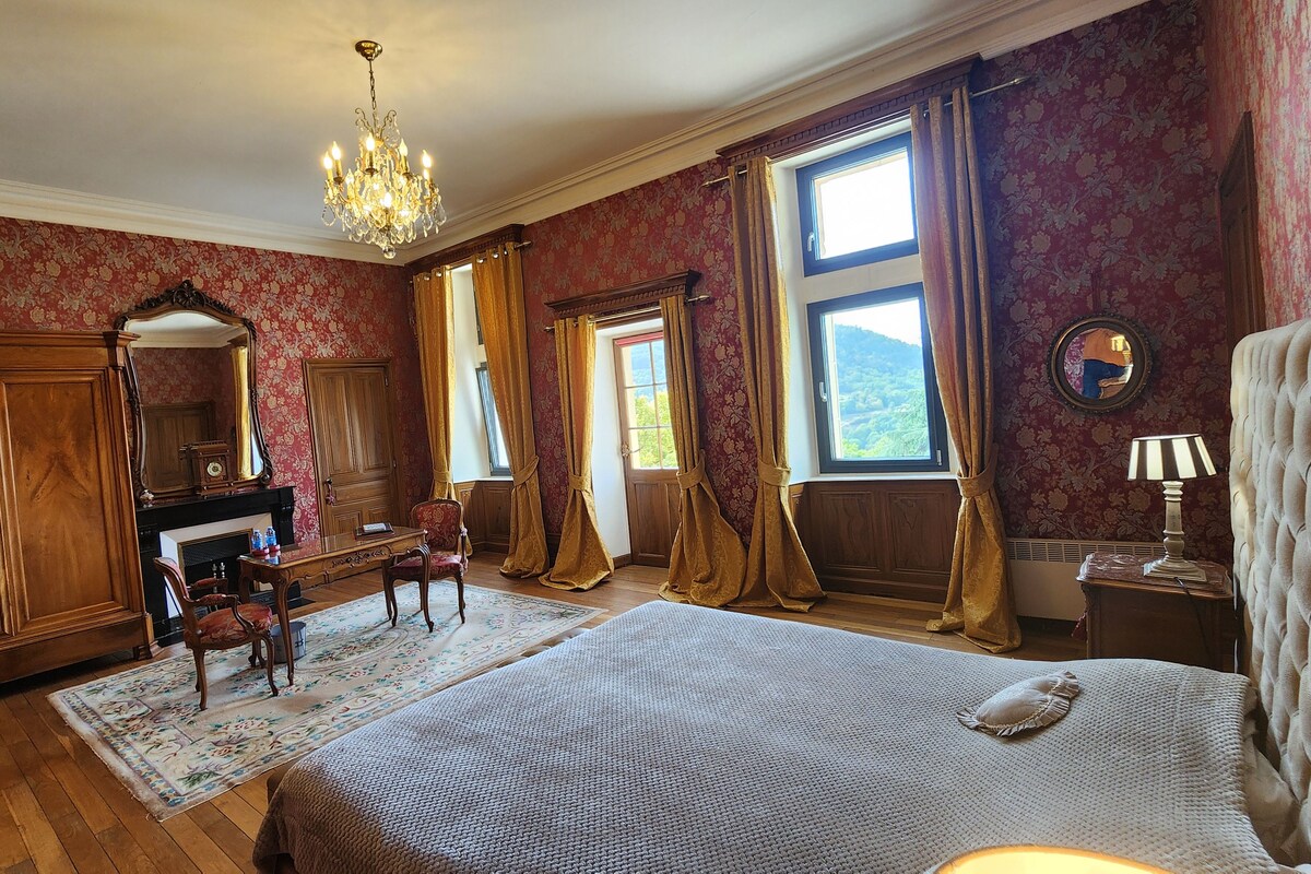 Quarto com cama, lareira, espelho, lustre e janela com cortinas.
