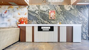 Bancada de recepção com parede de mármore, um quadro emoldurado e uma placa com a inscrição 'PALETTE Company-Serviced'.