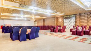 Uma sala de banquetes com teto de padrão geométrico, fileiras de mesas com cadeiras e piso estampado.