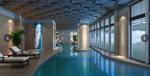 Piscina interna com design moderno no teto, cadeiras de descanso e grandes janelas.