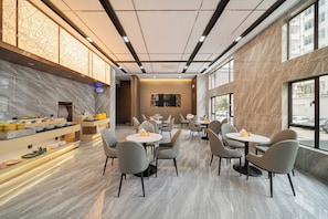 Uma área de jantar moderna com piso de mármore, cadeiras estofadas em cinza e um balcão de buffet com alimentos.