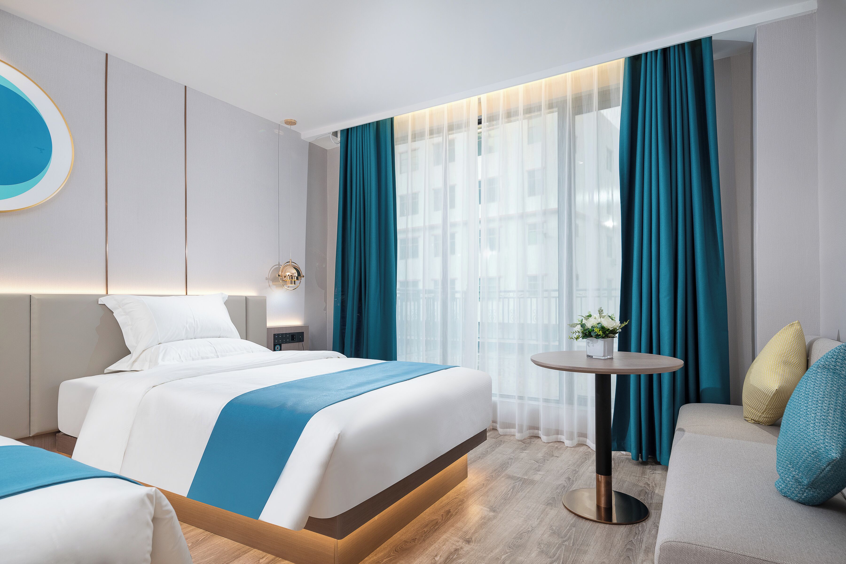 Quarto de hotel com cama, sofá, mesa pequena e janela com cortinas.