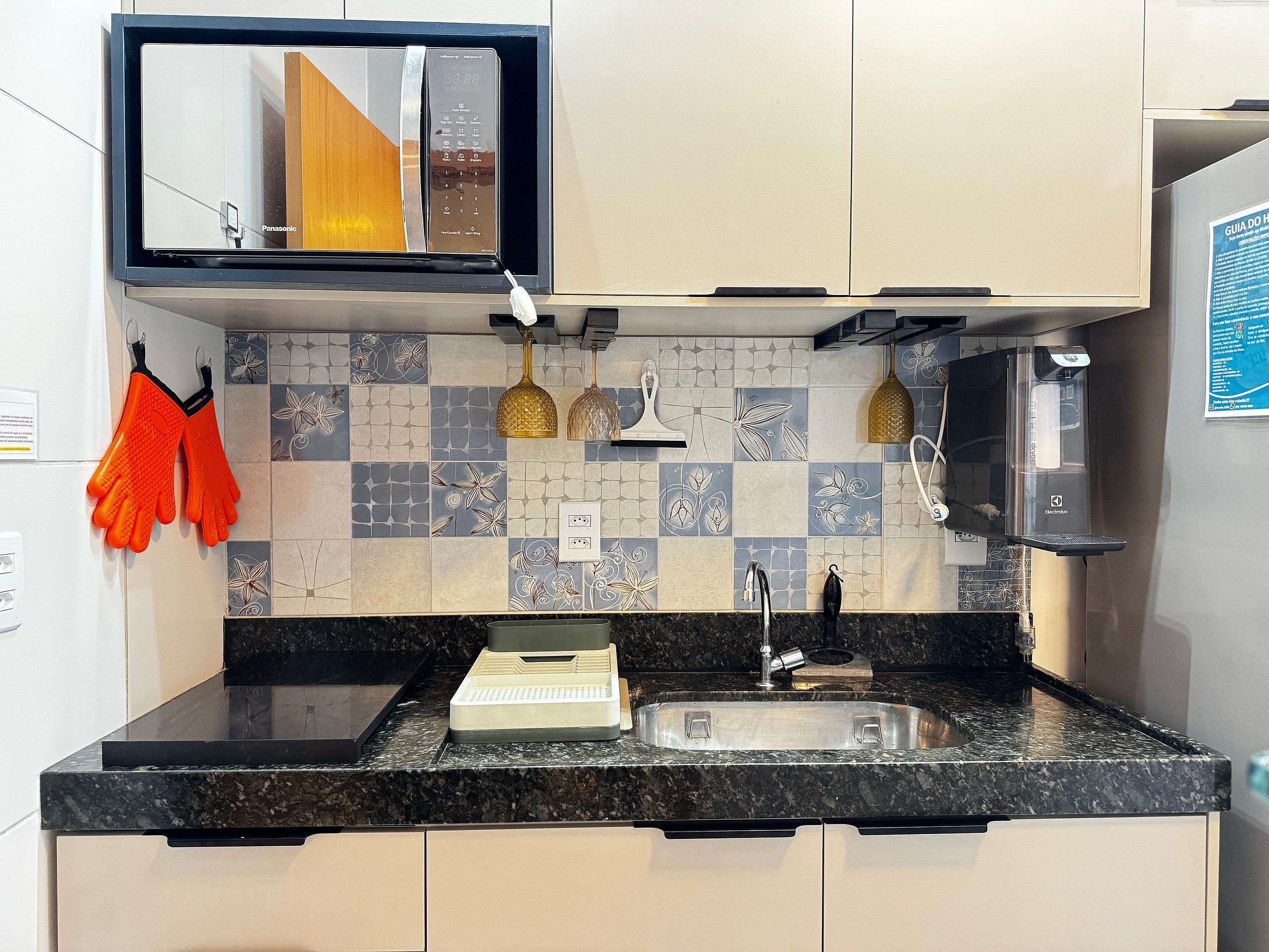 Uma cozinha com bancada preta, pia, micro-ondas e armário acima da bancada.