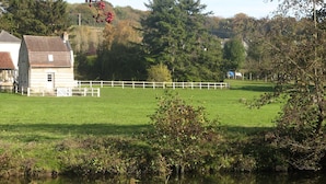 Paisagem rural com um lago, cerca branca e um edifício com telhado vermelho.