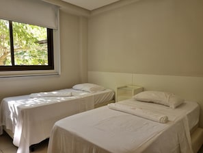Quarto com duas camas, janela com vista para vegetação e mesa de cabeceira com abajur.