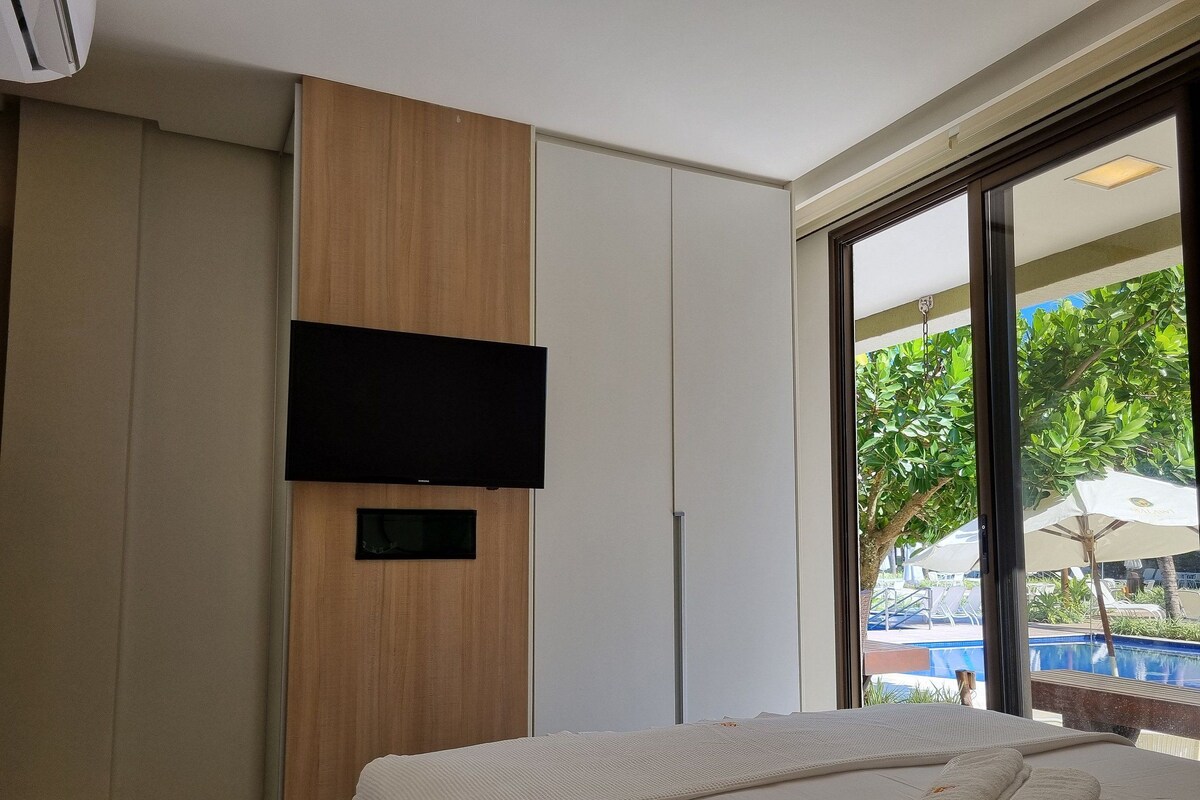 Quarto de hotel com cama, televisão presa na parede e uma grande janela com vista para o exterior.