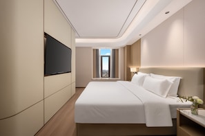 Quarto de hotel moderno com uma cama grande, uma televisão de tela plana na parede, mesa de cabeceira com abajur e vista para a cidade pela janela.