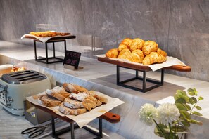 Buffet de café da manhã com pães, uma torradeira e um letreiro com código QR.