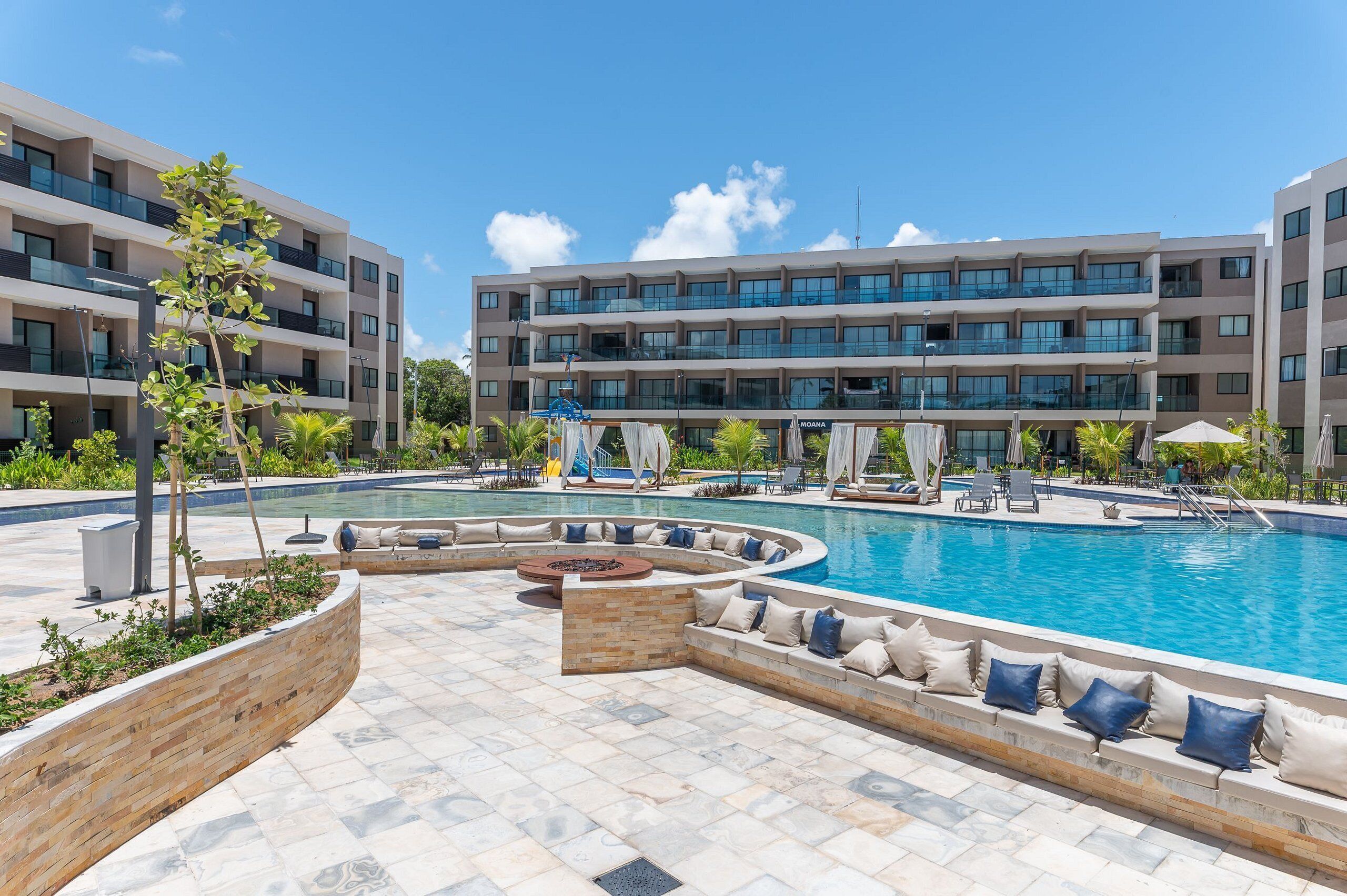 Um hotel moderno com área de piscina, espaço para sentar ao ar livre e céu azul.