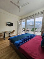 Um quarto com cama, escrivaninha, cadeira, televisão e varanda com vista.