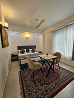 Quarto de hotel com cama, mesa de cabeceira, abajur, ventoinha no teto, janela com cortinas e um tapete.