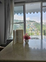 Um quarto com uma janela grande, um livro e um vaso de flores.