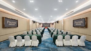 Uma sala de conferências com fileiras de mesas e cadeiras, um palco na frente e placas com o nome 'POLITTON'.
