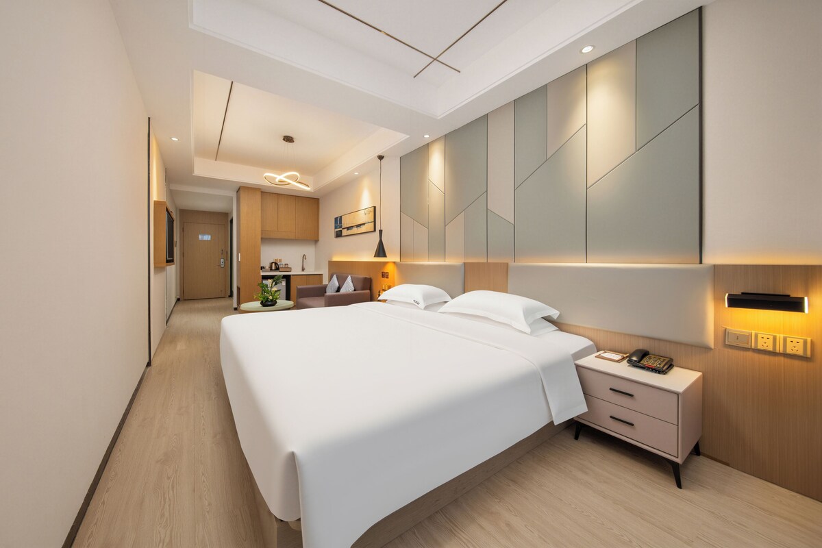 Quarto de hotel moderno com cama grande, mesas de cabeceira, escrivaninha e área de estar.