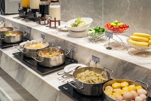 Buffet variado com diversos pratos, incluindo dumplings, legumes e frutas.