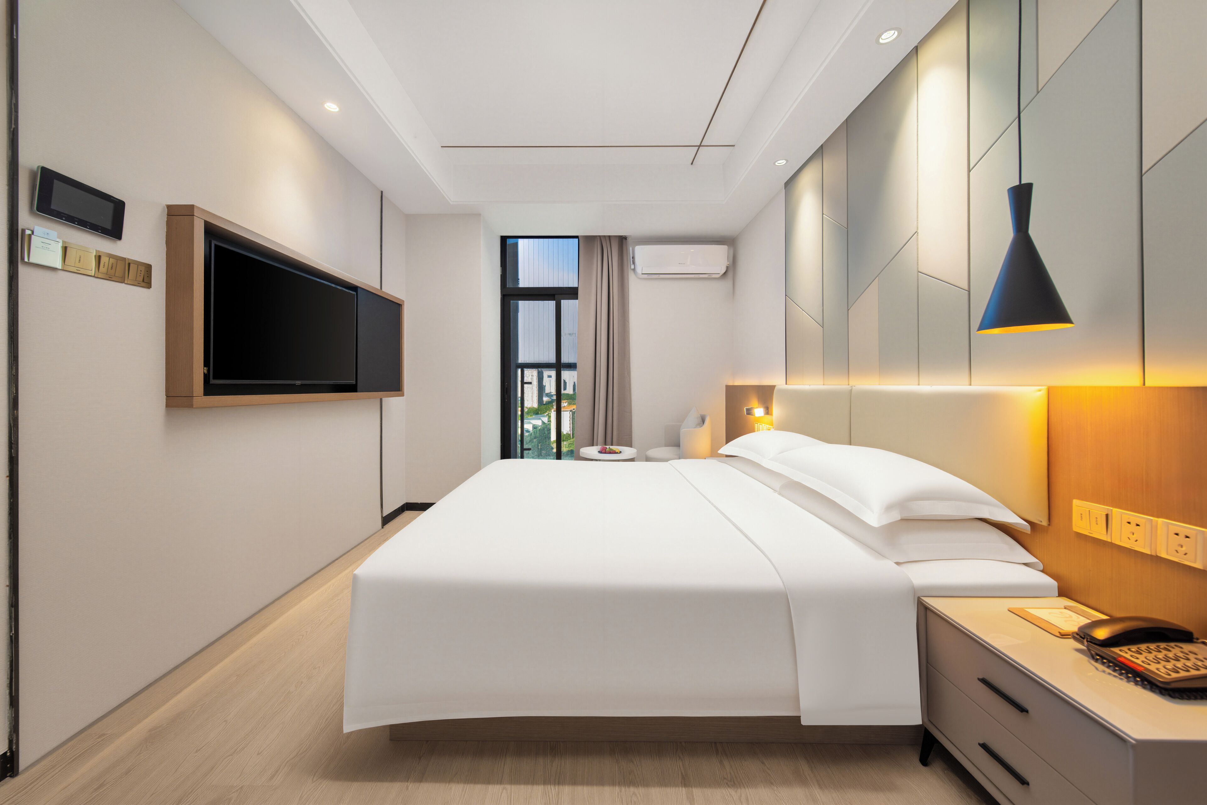 Quarto de hotel moderno com cama grande, televisão de tela plana, mesa de cabeceira com abajur e janela com vista.