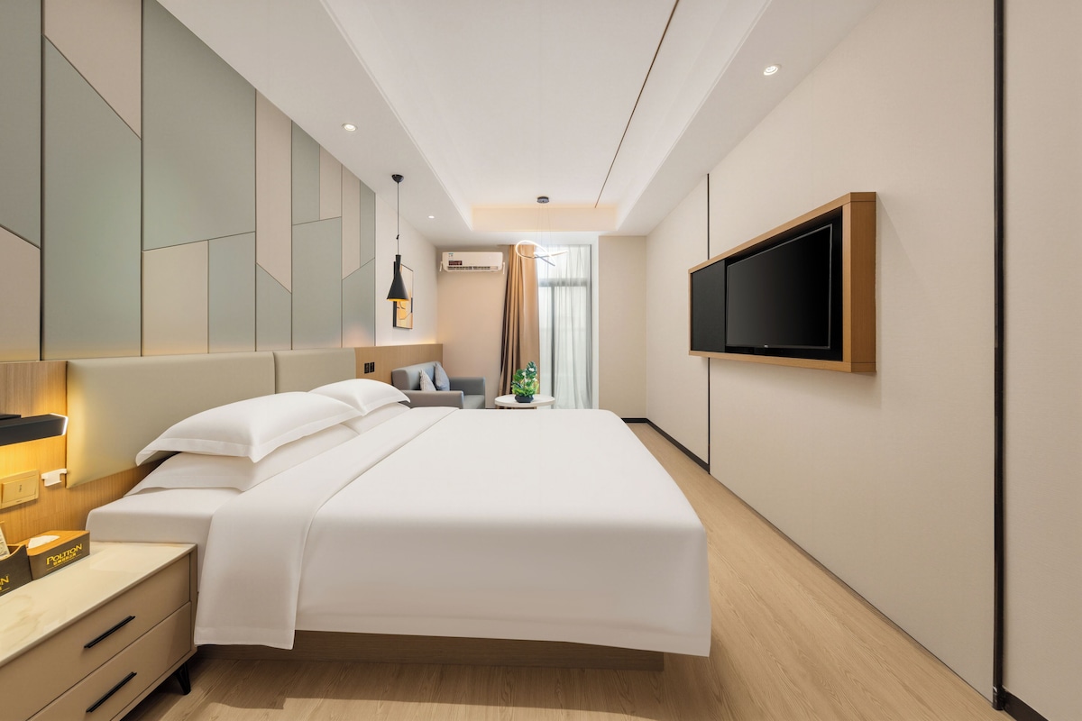 Quarto de hotel moderno com uma cama grande, televisão de tela plana, mesa de cabeceira e guarda-roupa.