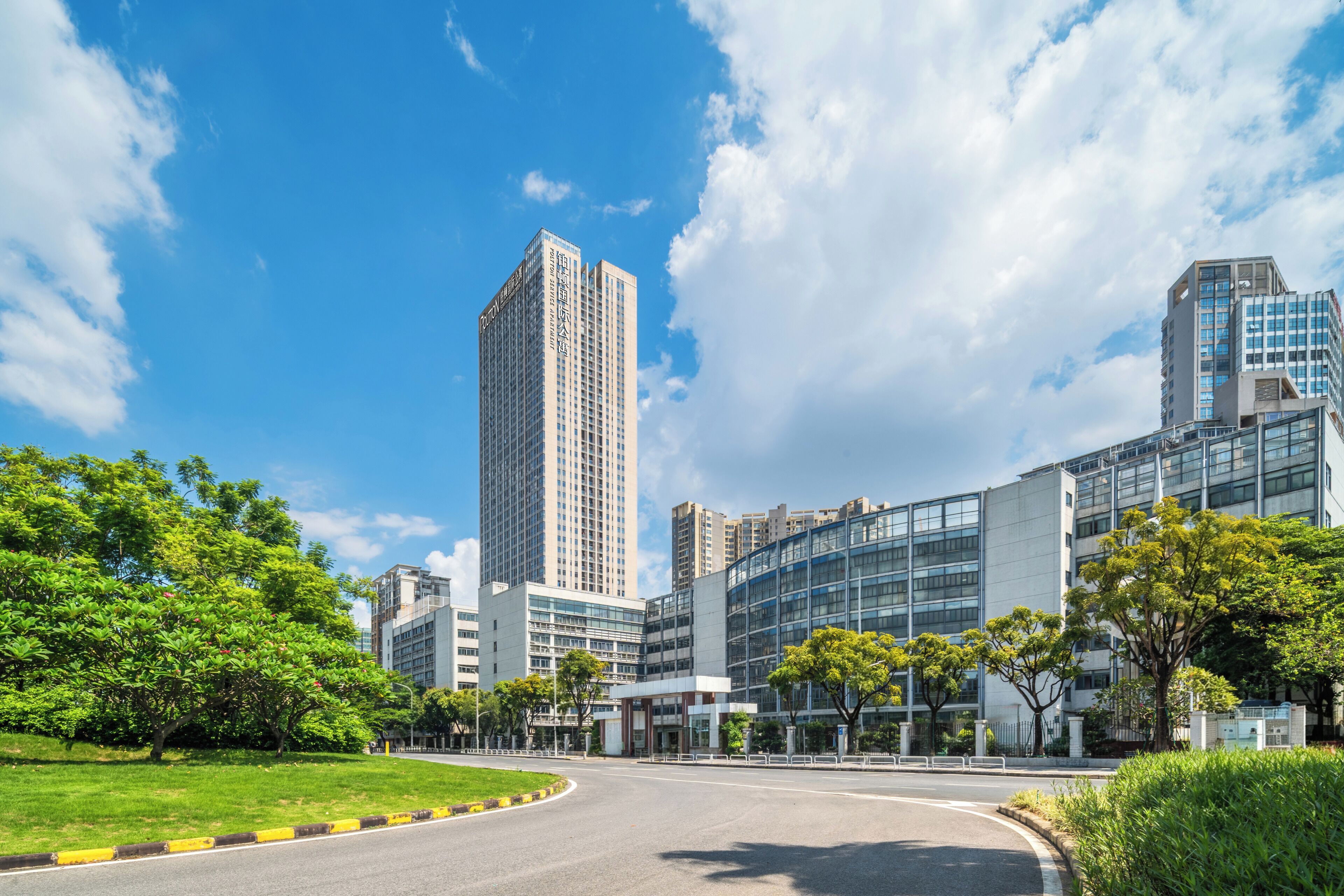 Um edifício moderno com uma torre imponente, rodeado por vegetação e uma estrada curva.