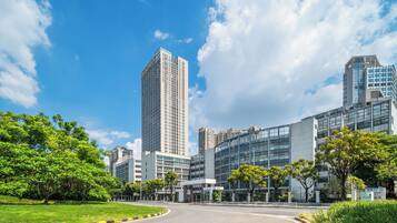 Um edifício moderno com uma torre imponente, rodeado por vegetação e uma estrada curva.