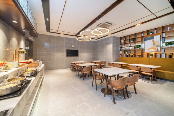 Um restaurante moderno com piso de mármore, mesas e cadeiras de madeira, área de buffet e uma parede com estantes de livros.
