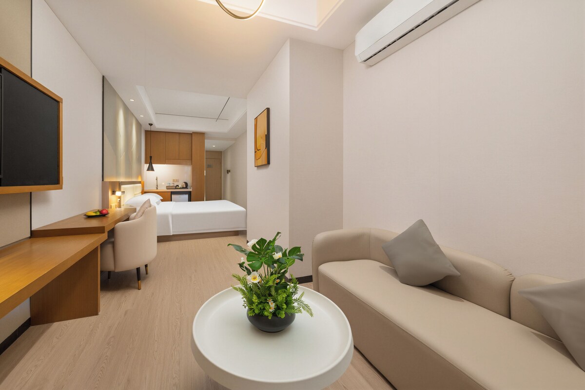 Quarto de hotel moderno com cama, sofá, escrivaninha e televisão.