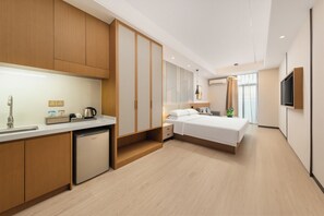 Quarto de hotel moderno com cozinha compacta, uma cama, mesa de cabeceira e televisão na parede.