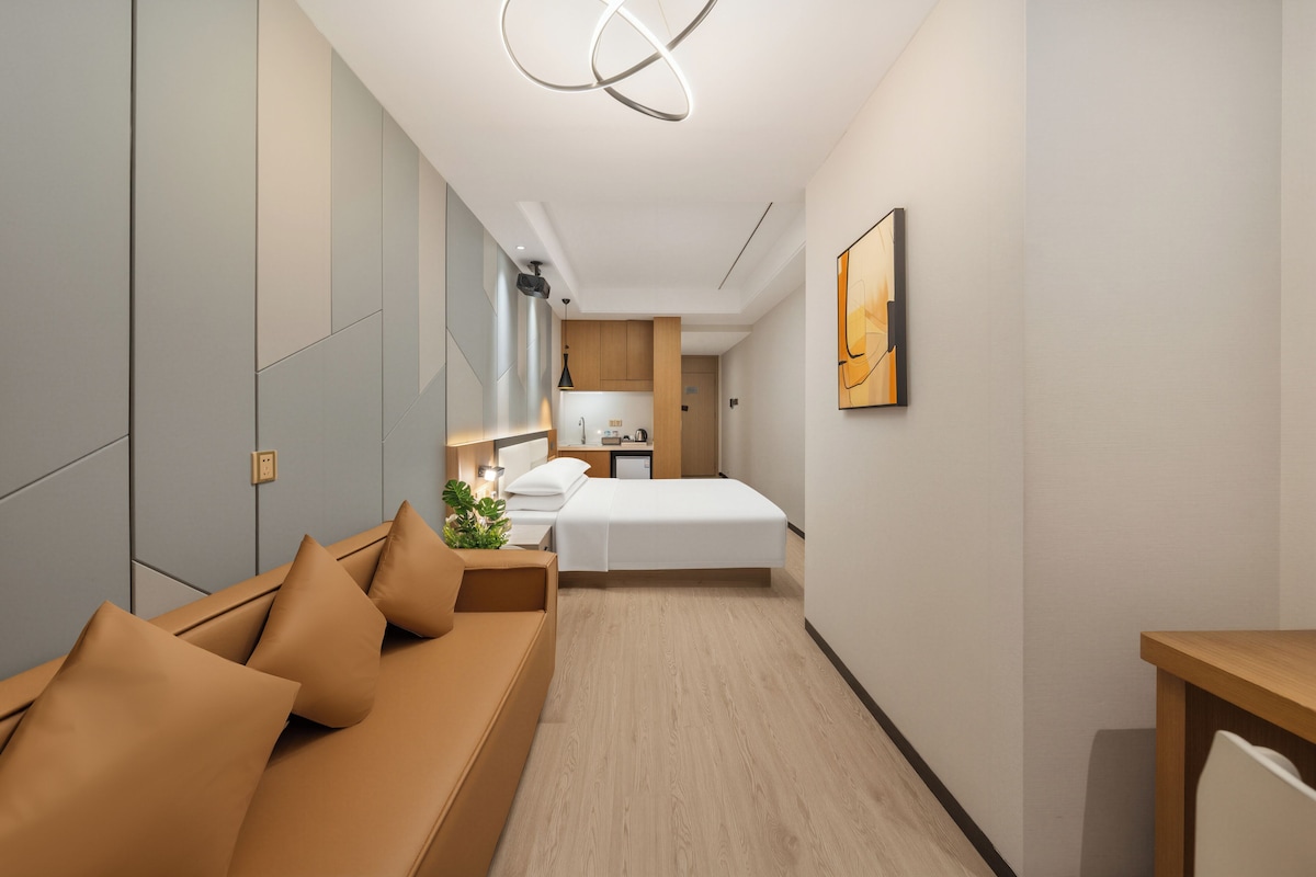 Quarto de hotel moderno com sofá, cama, escrivaninha e um quadro na parede.