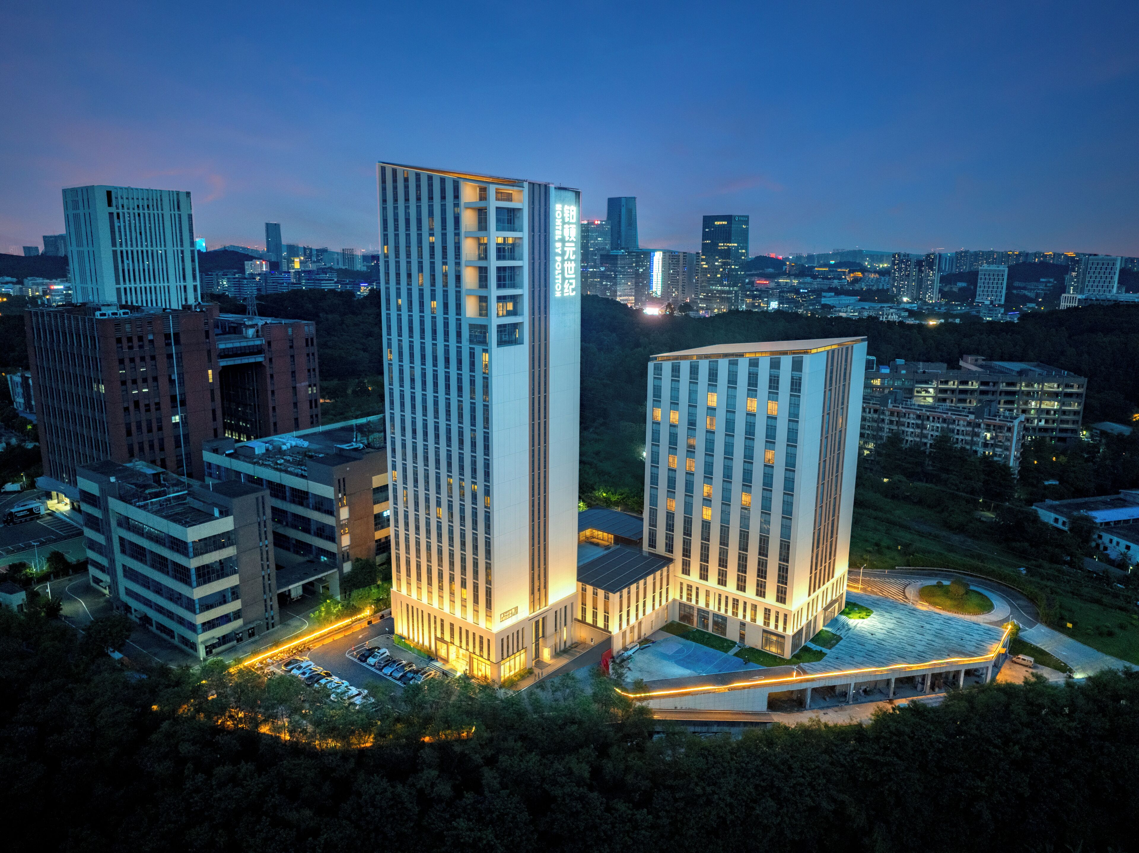 Um edifício alto com design arquitetônico moderno, cercado por outros edifícios e um estacionamento.