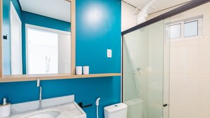 Um banheiro com parede azul, pia branca, espelho e box de vidro.