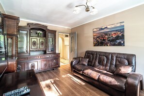 Sala de estar com sofá de couro marrom escuro, um aparador de madeira e um quadro de uma paisagem urbana.