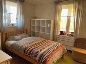 Um quarto com uma cama de solteiro, um guarda-roupa branco, uma mesinha e uma cadeira.