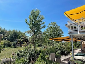 Um jardim com diversas plantas e um toldo amarelo sobre uma varanda.