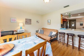Uma sala de estar aconchegante com sofá, mesa de jantar e cadeiras, cozinha com geladeira e balcão com banquetas.