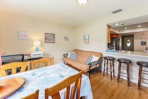 Uma sala de estar aconchegante com sofá, mesa de jantar e cadeiras, cozinha com geladeira e balcão com banquetas.